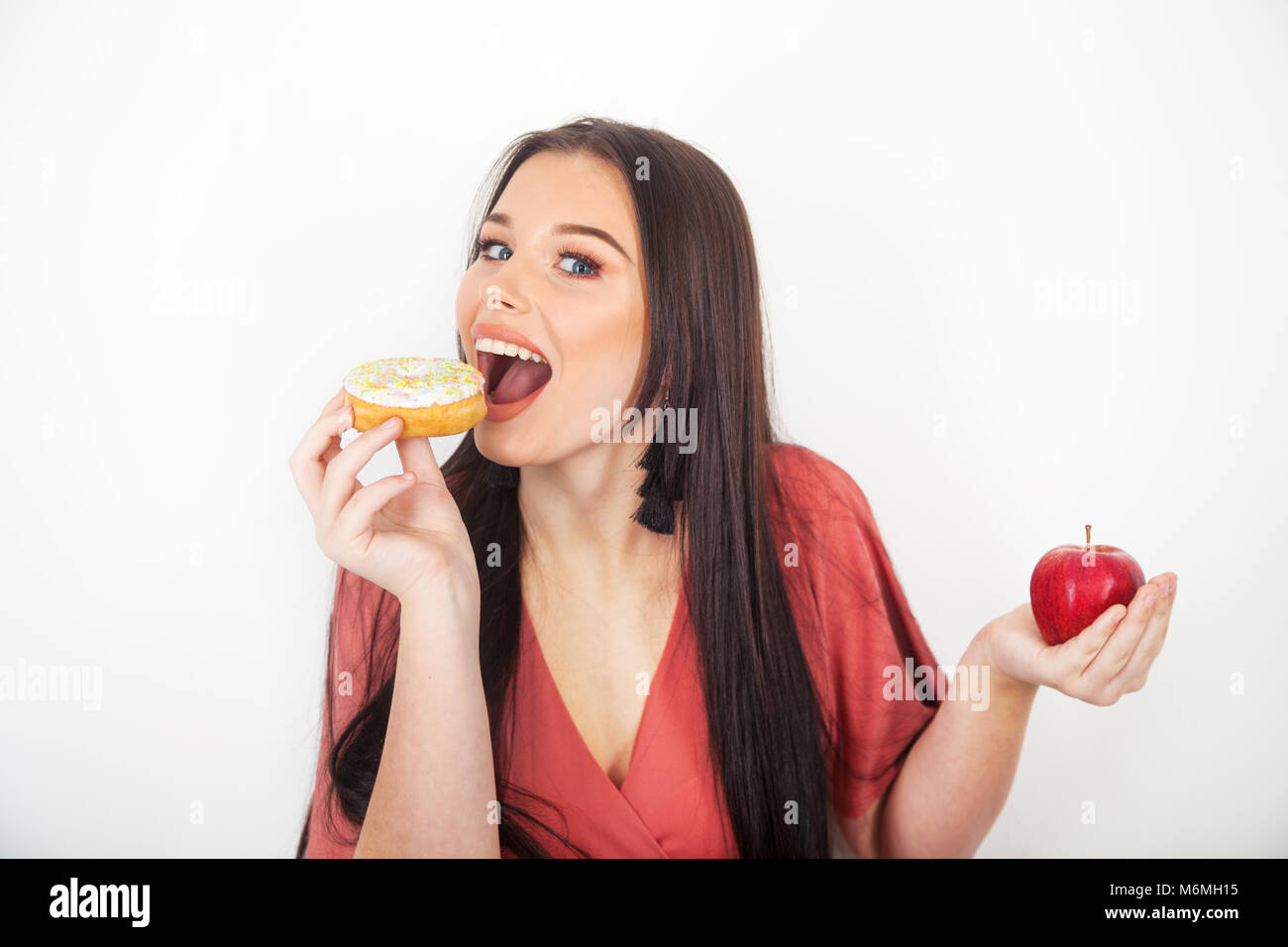 Pretty teenage girl taking a bite out of a donut and holding an apple ...