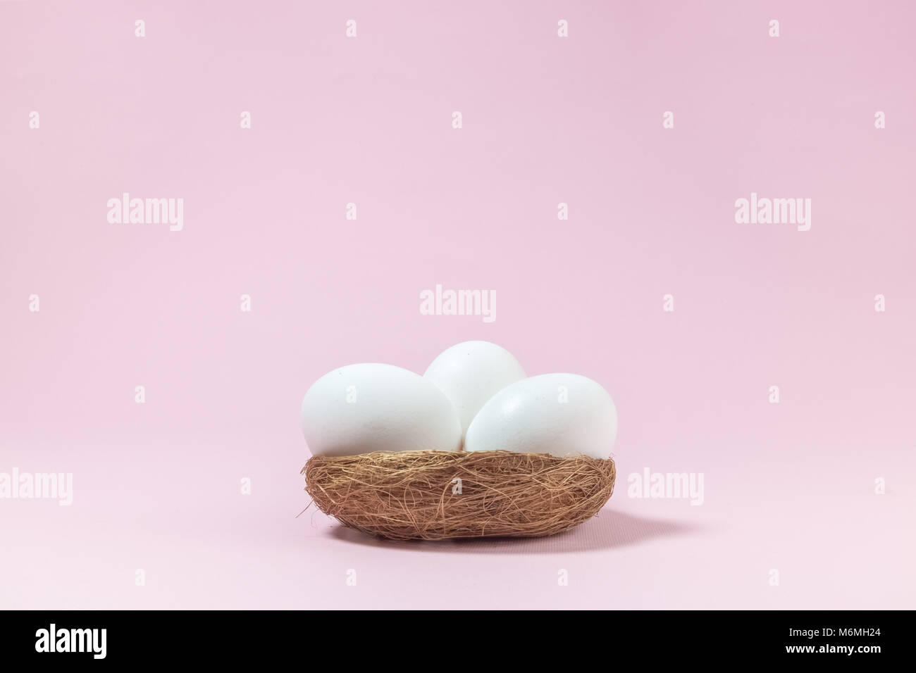 Close up of white eggs in nest on plain pink pastel background. Minimal ...