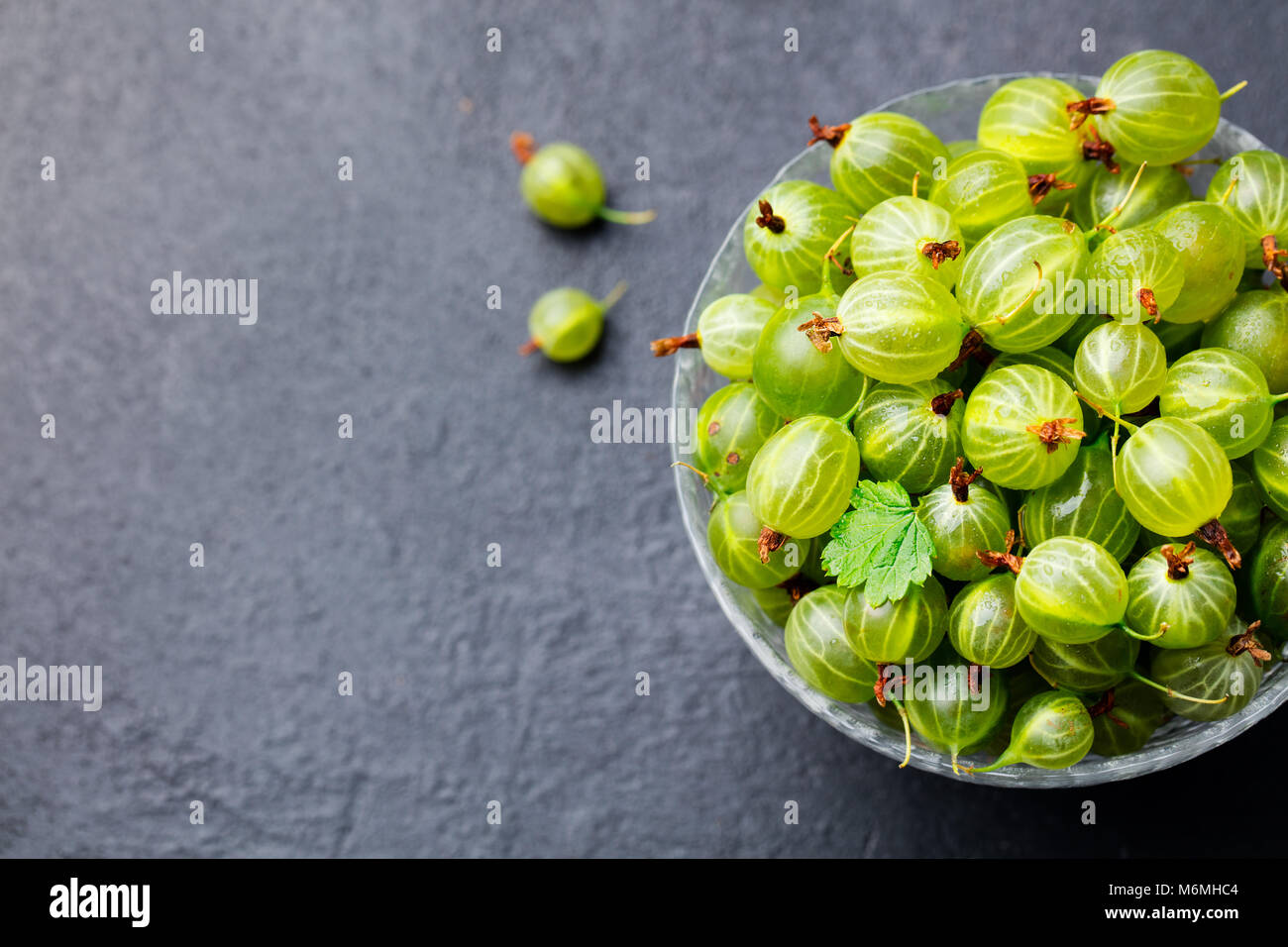Gooseberries in glass bowl on black stone slate background. Top view ...