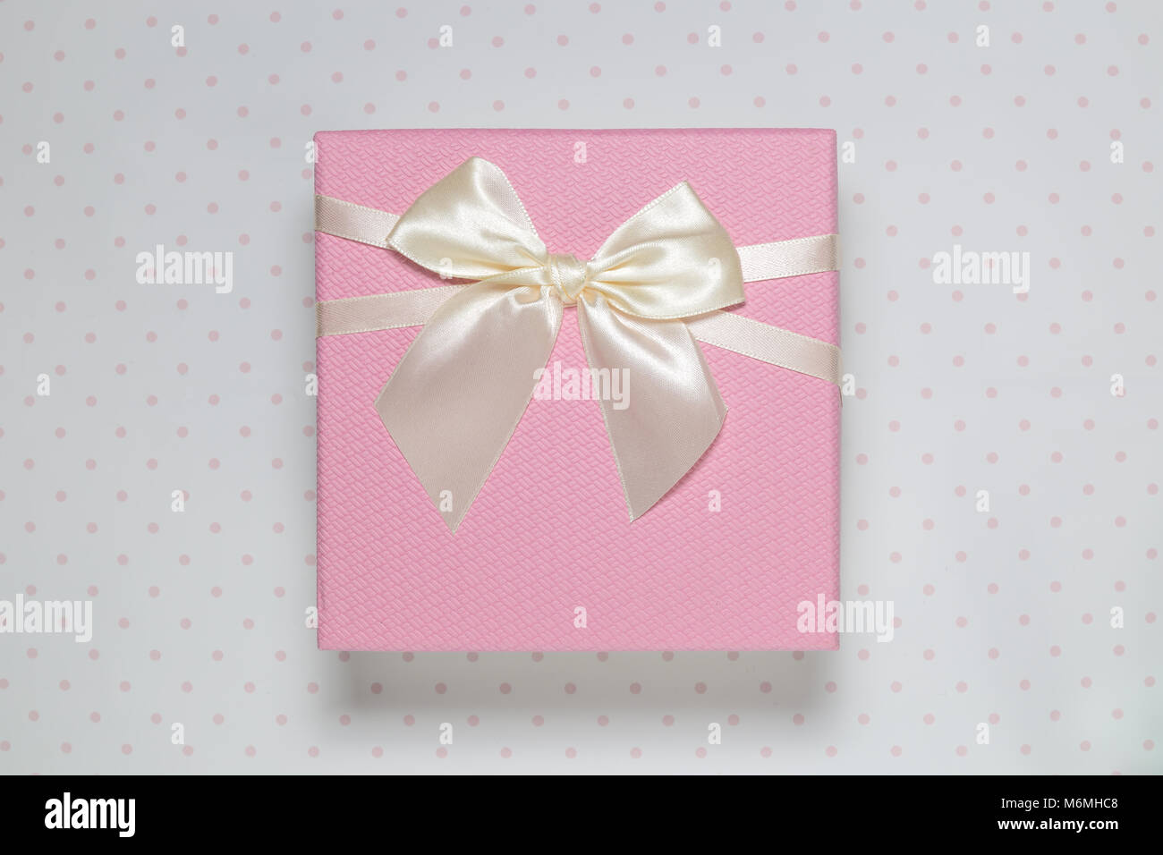 Plain pink rose gift box with tie on bright polka background minimal ...