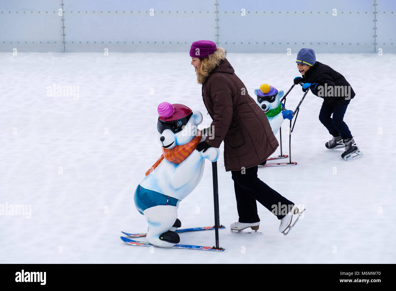 Woman and child having fun skatimg on a public ice rink using a frame ...
