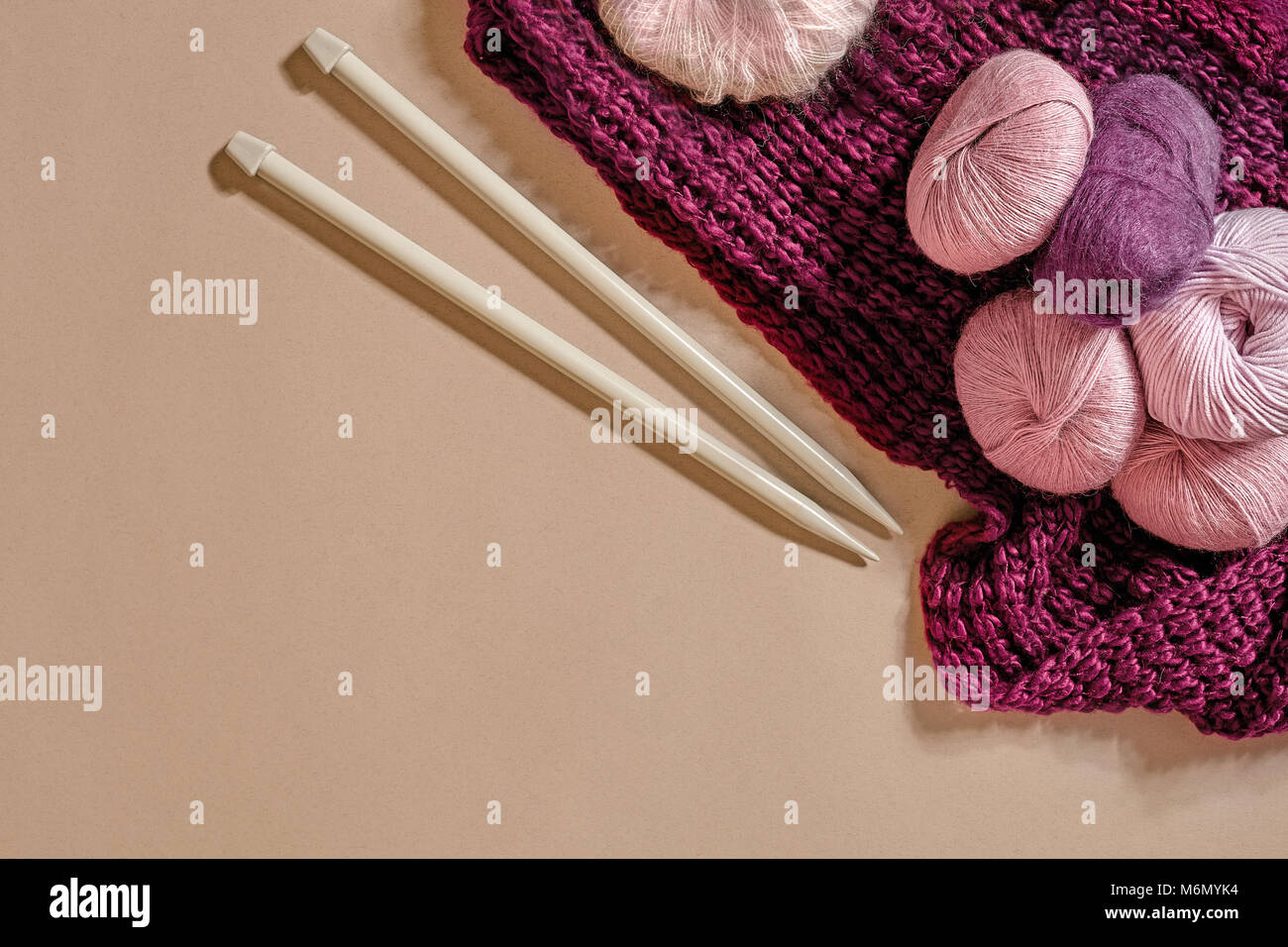A group of colored balls of yarn and knitting needles on a beige ...