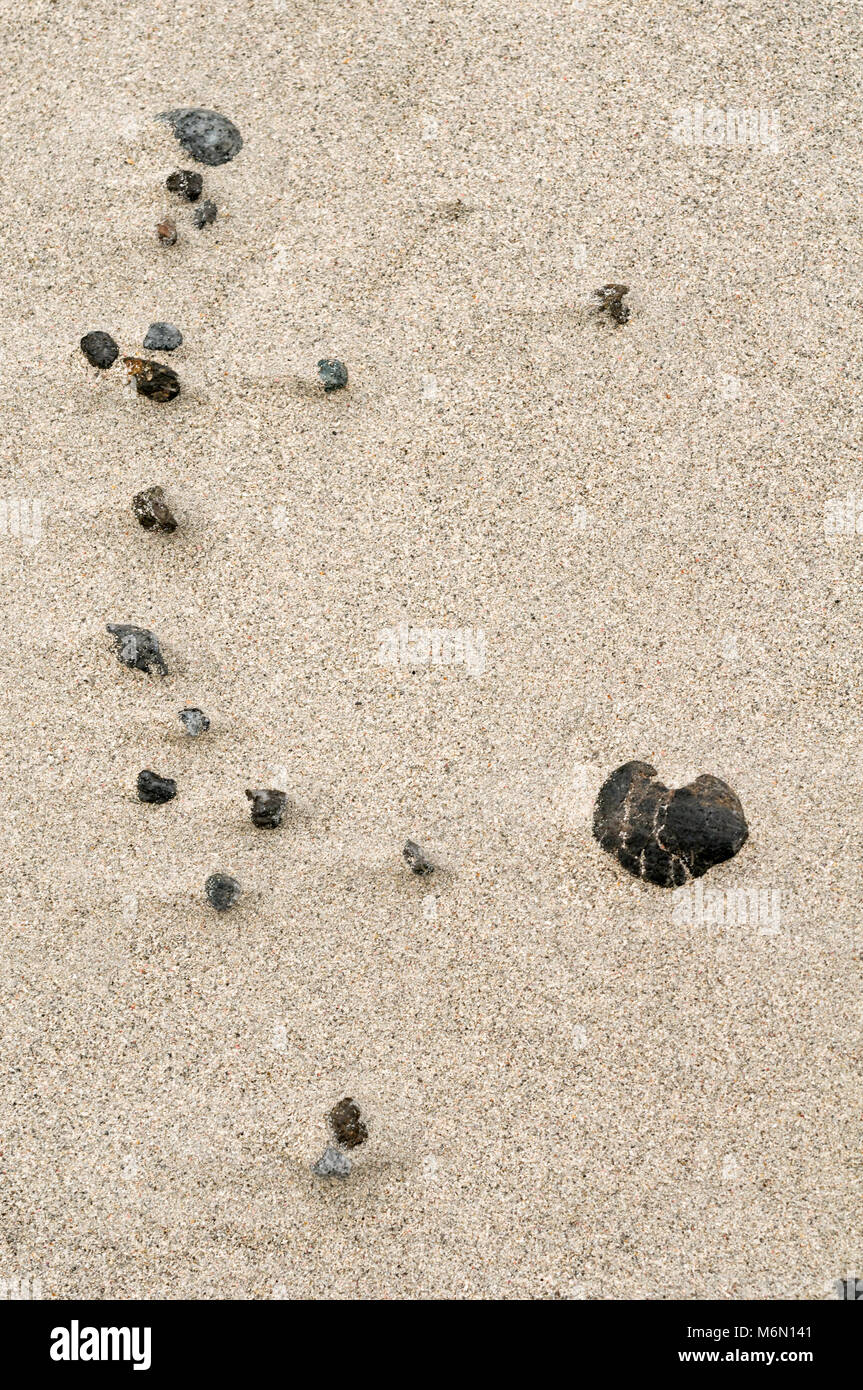 Heart-shaped pebble and lots of little pebbles on a sandy beach showing ...