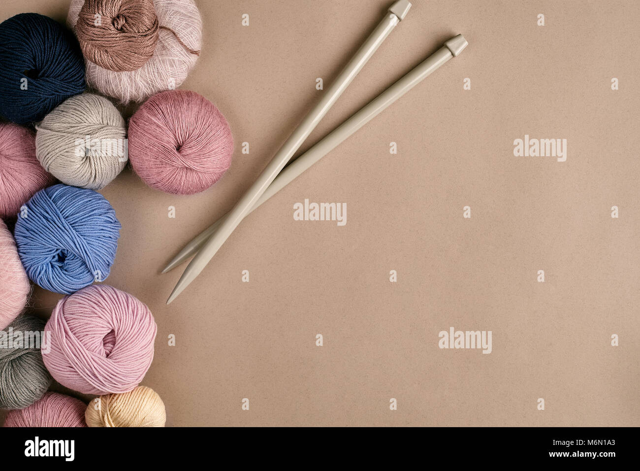 A group of colored balls of yarn and knitting needles on a beige ...