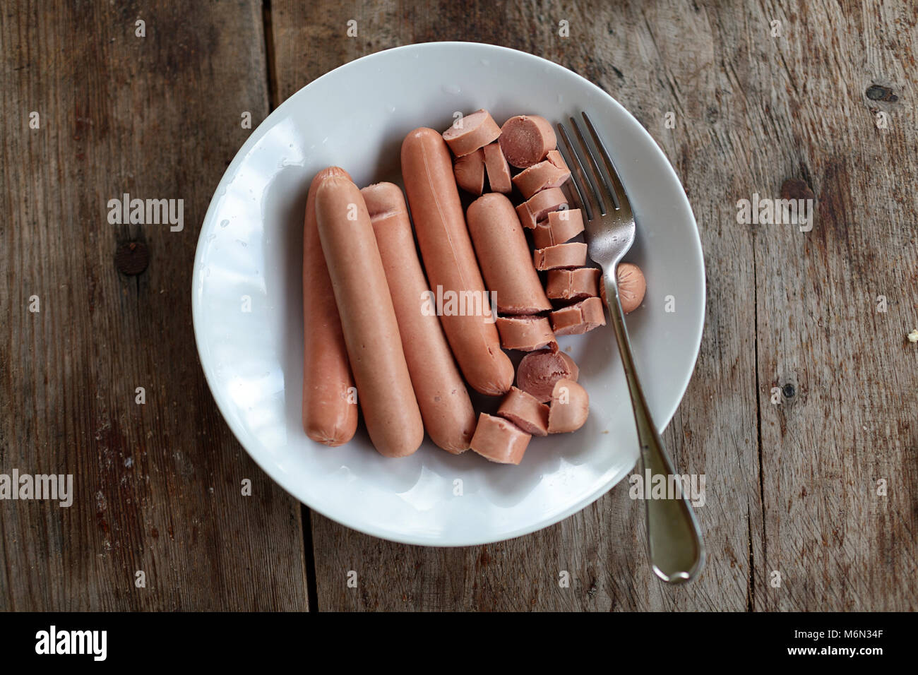 Hot dog chopped on white plate with vintage fork on rustic wooden table ...