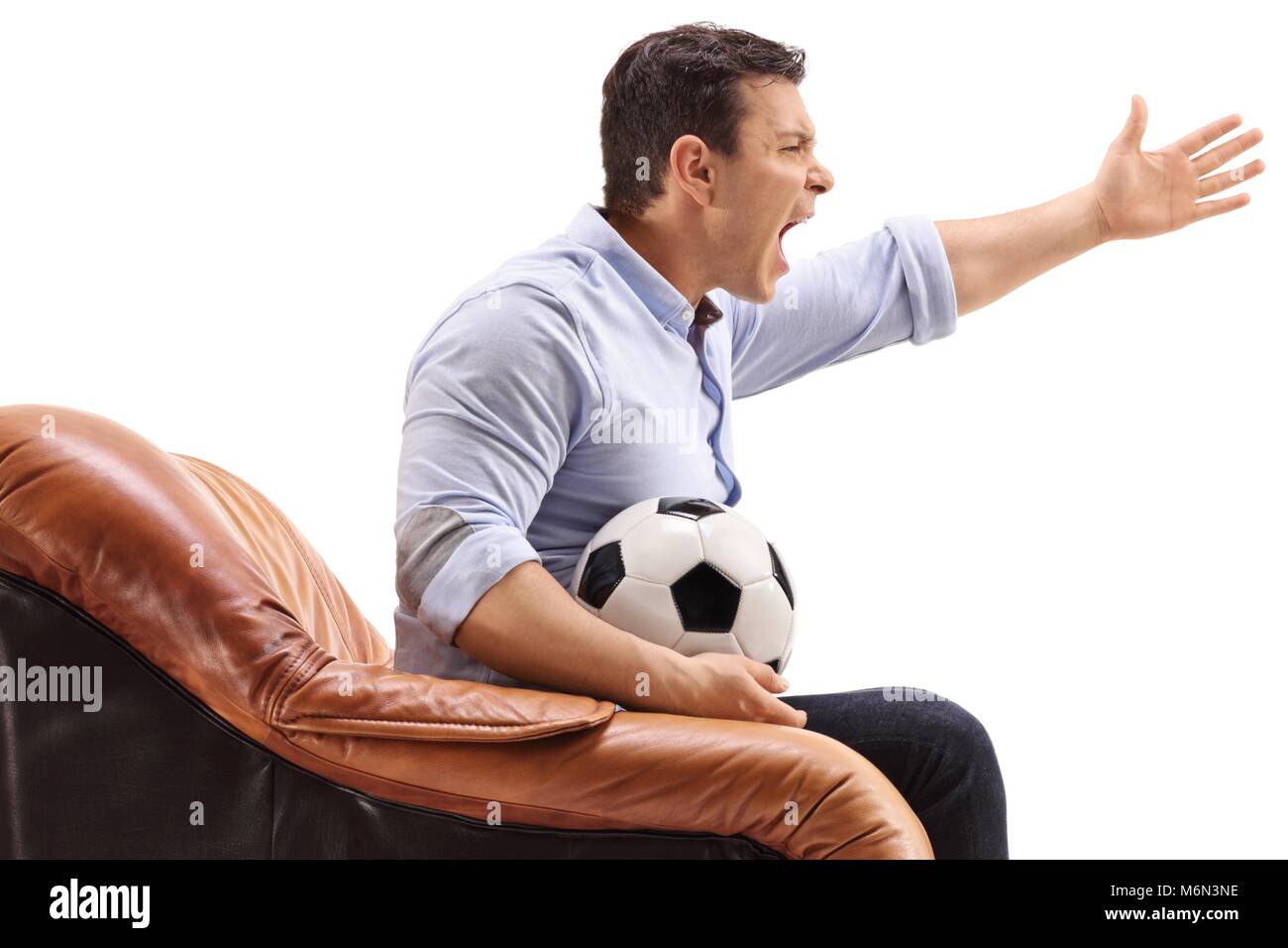 Angry young man with a football sitting in an armchair and yelling ...