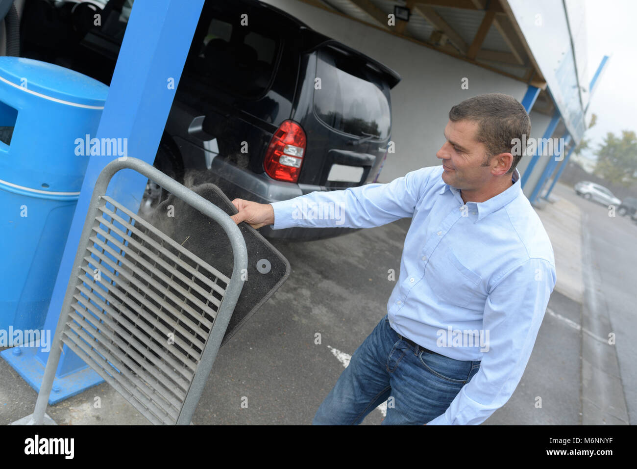 man shaking car mats Stock Photo - Alamy