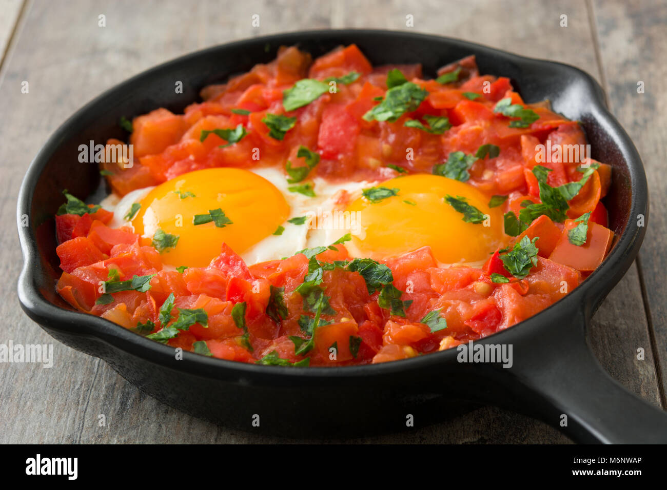 Shakshuka in iron frying pan on wooden table. Typical food in Israel ...