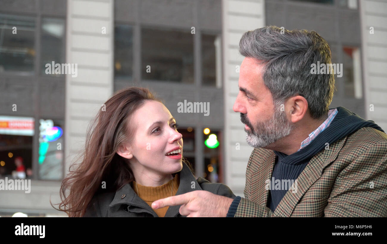 Two friends having discussion at night sitting on bench along busy city ...