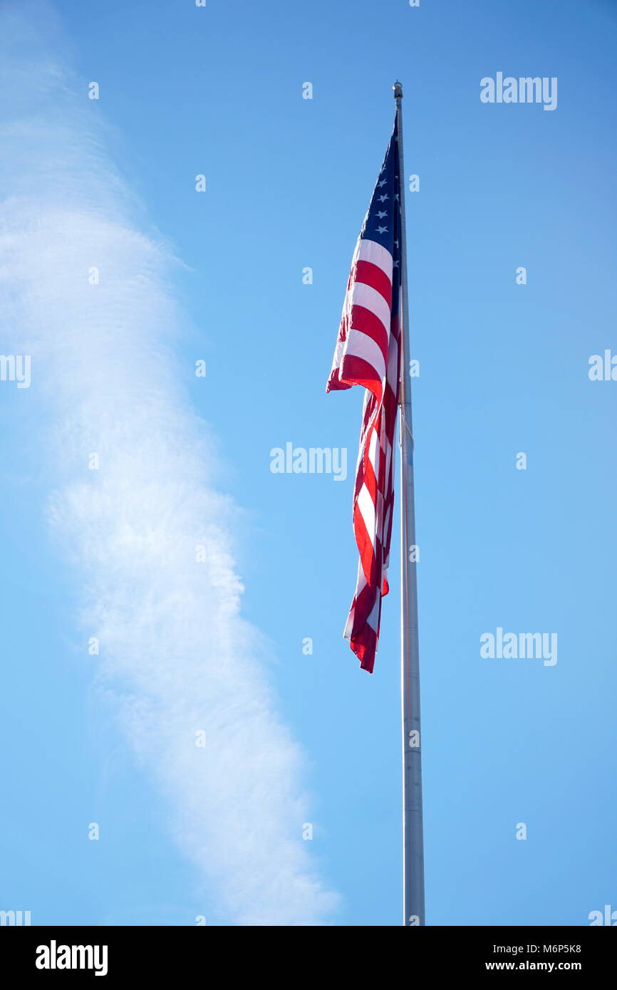 American flag flying high on pole with no wind on a sunny bright day ...