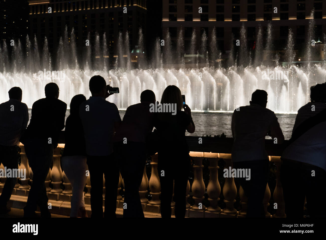 Silhouette of people at night watching illuminated dancing fountain ...