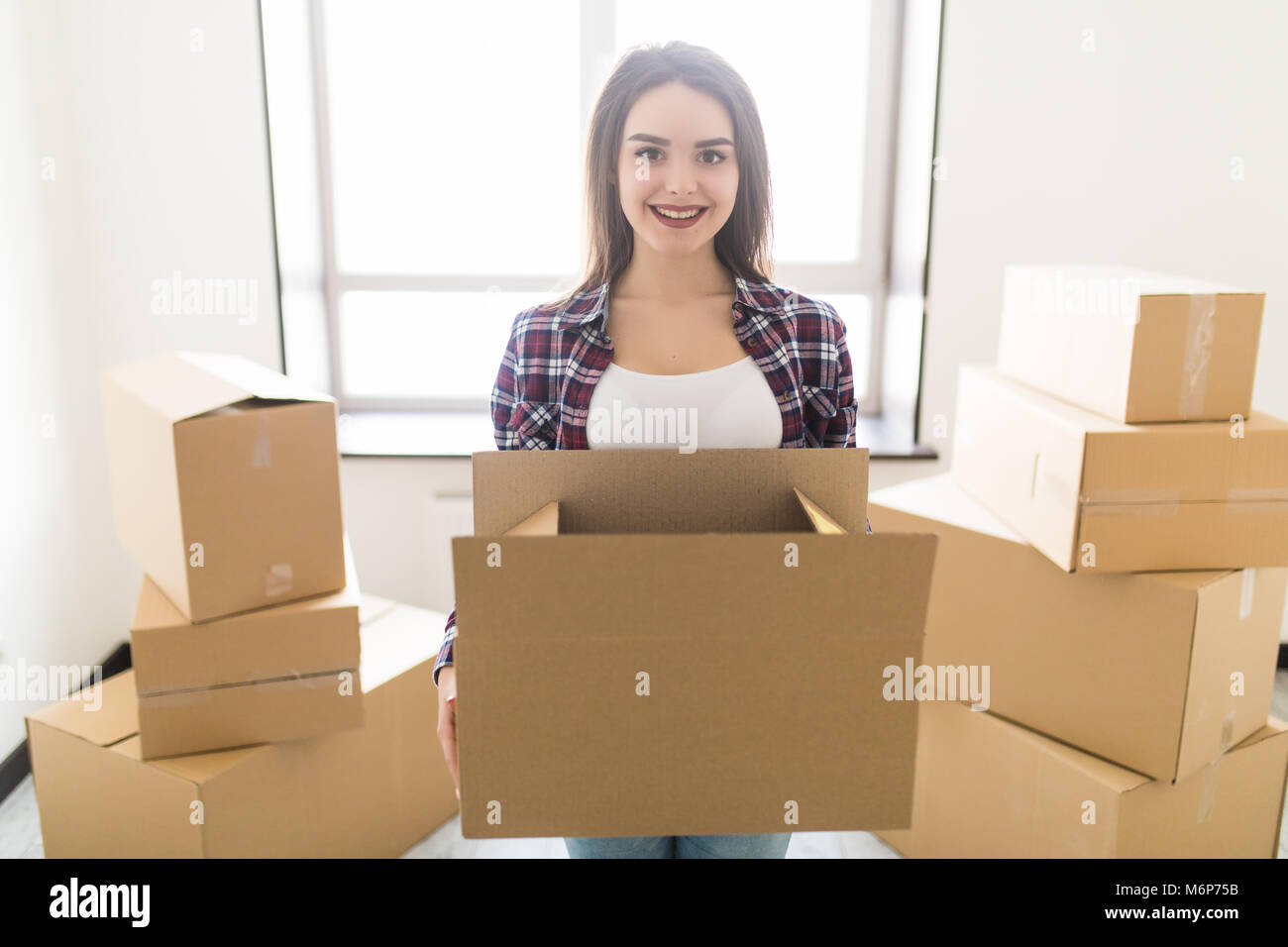 Young happy woman carrying a pile of cardboard boxes in her new ...