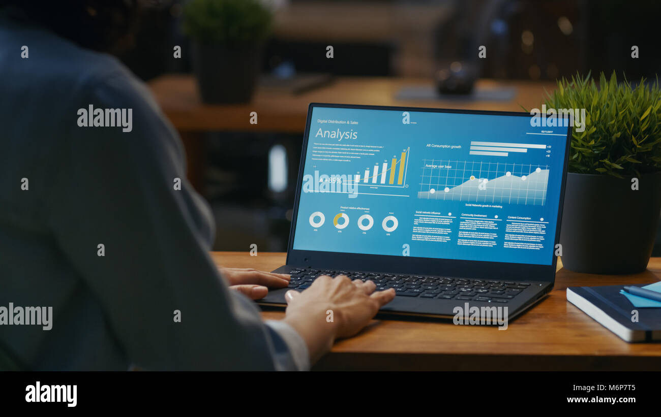 Female Analyst at Her Desk Works on a Laptop Showing Statistics, Graphs ...