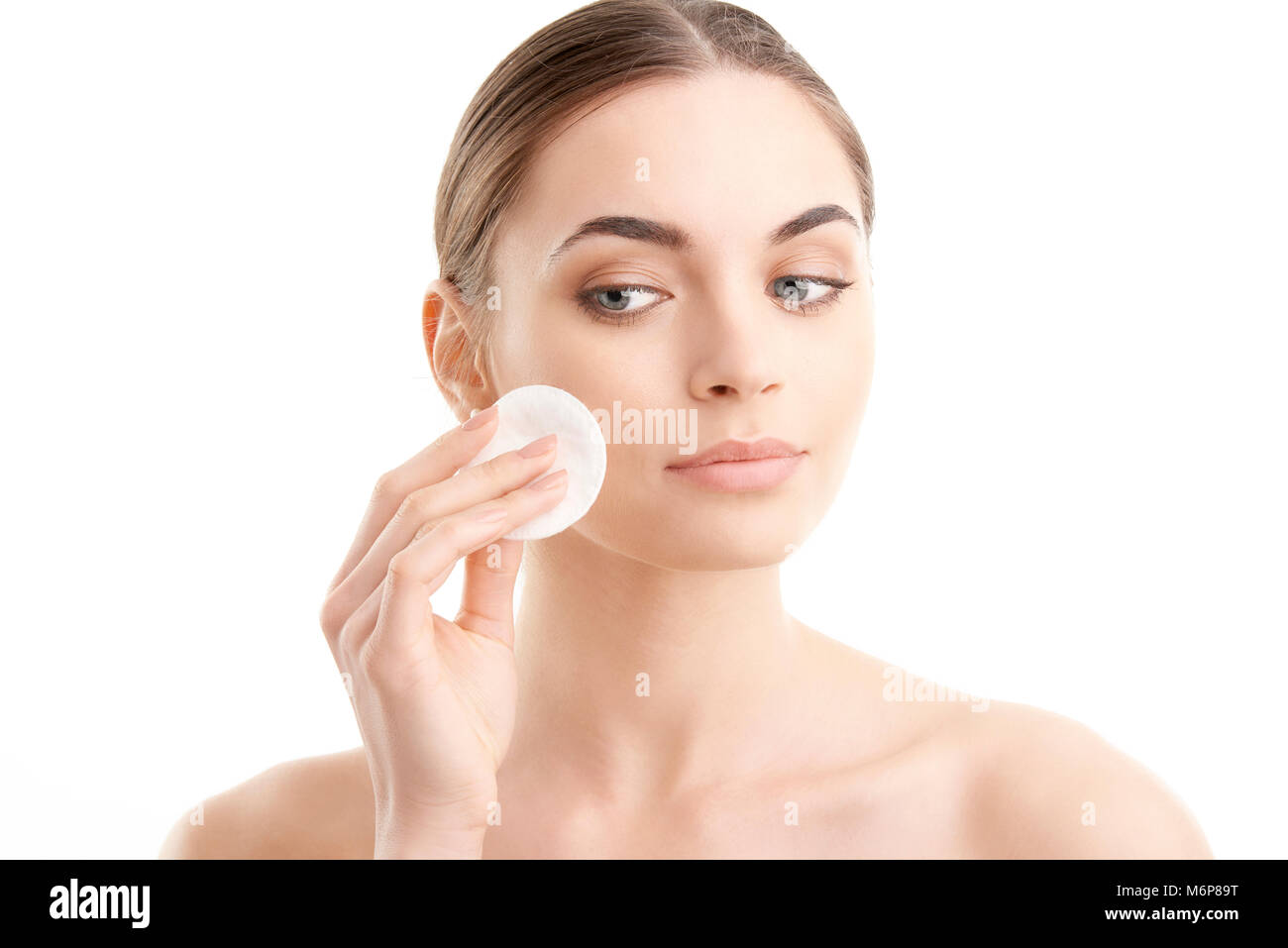 Beautiful young woman using cotton pad while cleansing her face ...