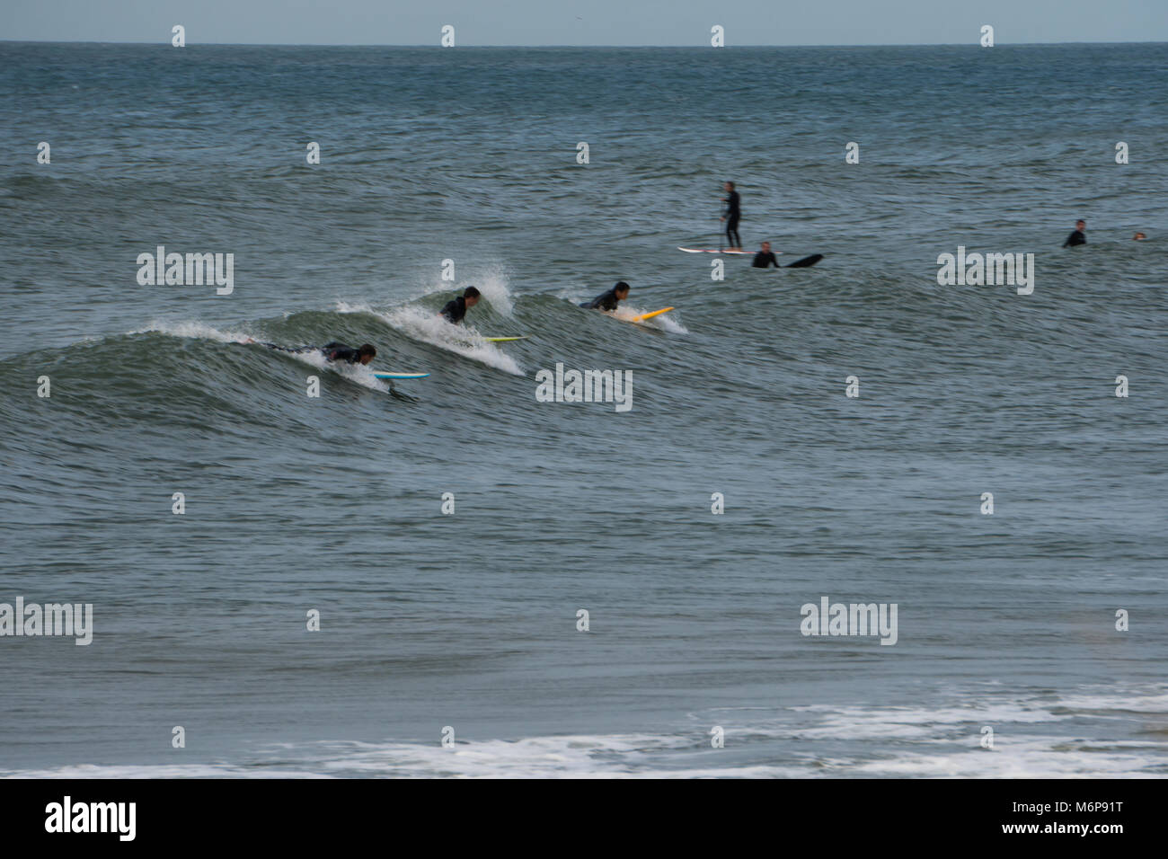 Row of surfers catching a big wave in the ocean at the beach. Fast ...