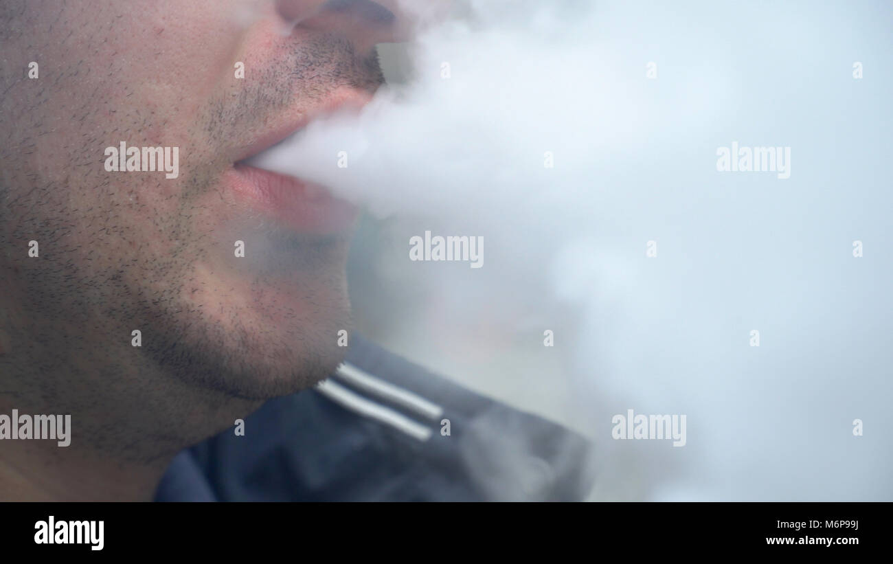 Young white male blowing vape smoke out of mouth outside on city street ...