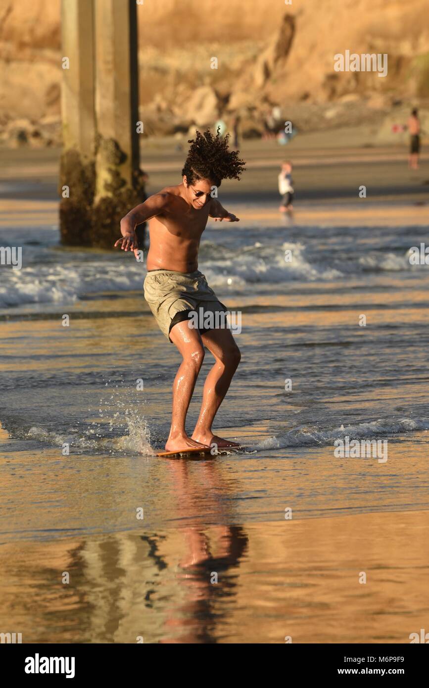 Young African-American man on a skim board, skimming, at beach during ...