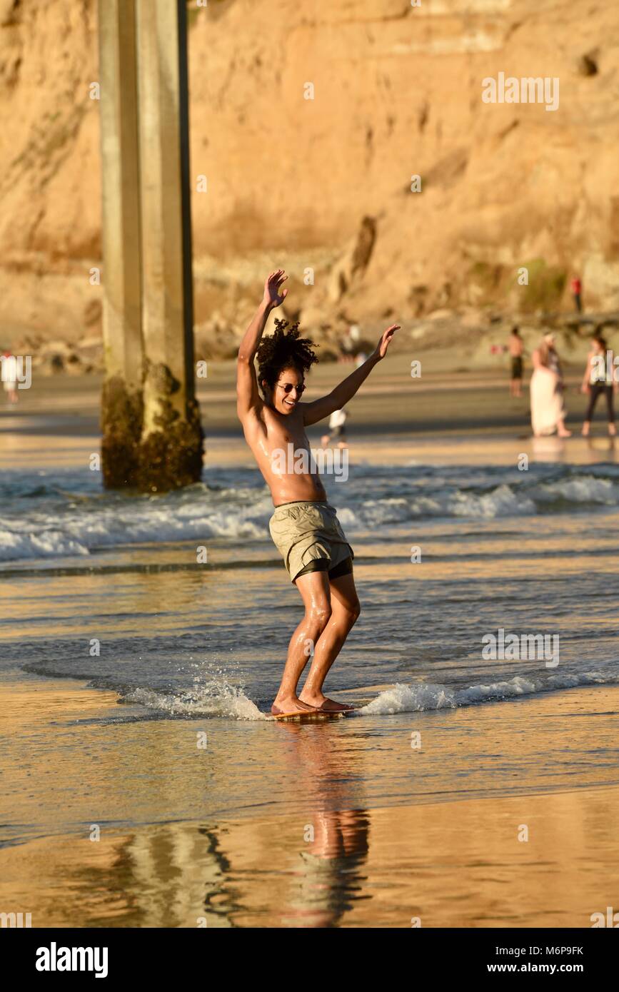 Young African-American man on a skim board, skimming, at beach during ...