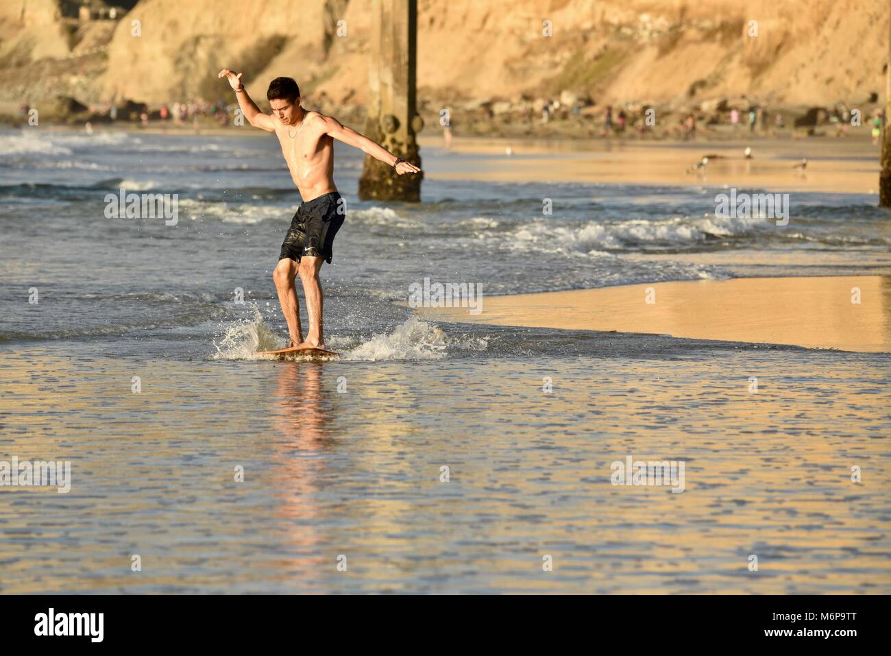 Young man on a skim board, skimming, at beach during sunset, gliding ...