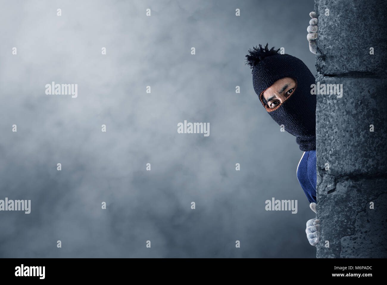 Robber hiding behind a empty wall with space for text Stock Photo - Alamy