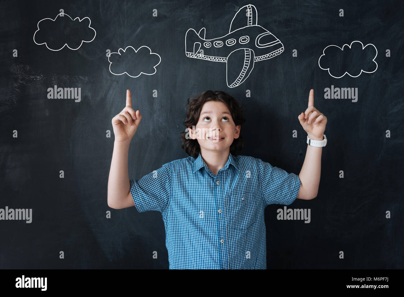 Emotional boy thinking of travelling by plane and pointing to the sky ...