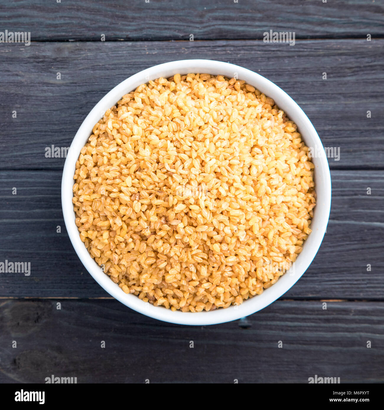 Uncooked bulgur in blue bowl on wooden table background. Dry bulgur ...