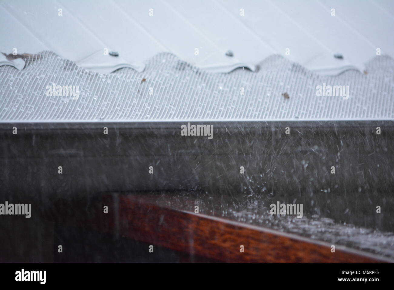 Raining, heavy rain drops falling, bouncing off the rooftop gutter and ...
