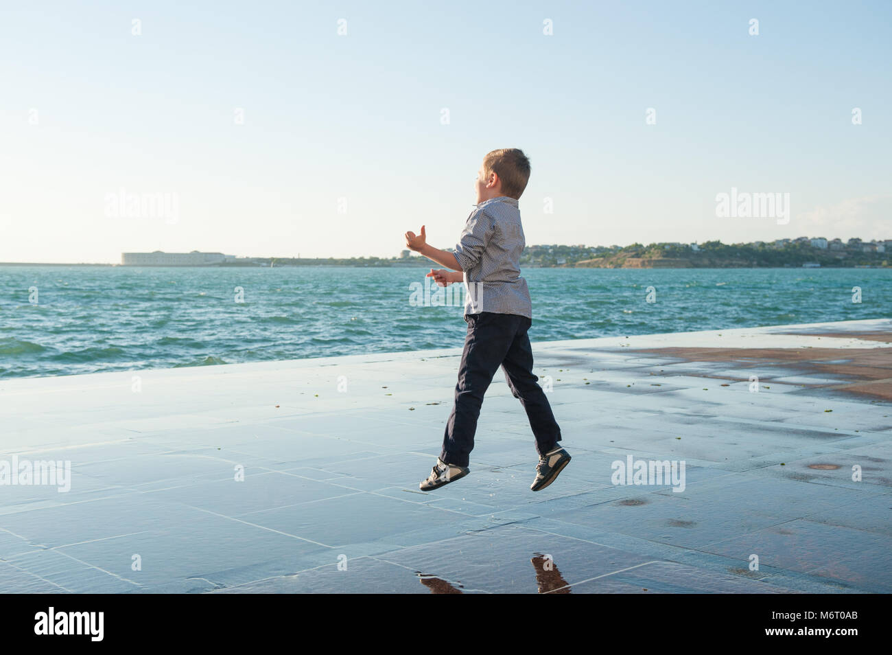 healthy small boy jumping high in the city against the sea in spring ...
