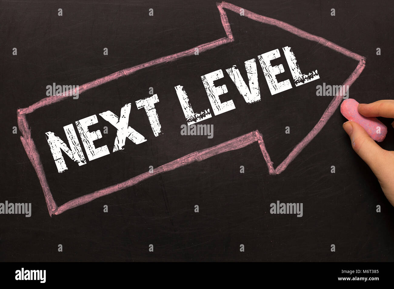 Next Level - female hand with chalk and arrow on blackboard background ...