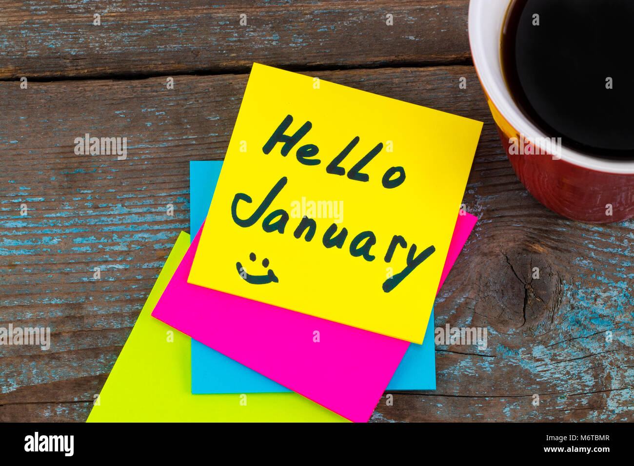 Hello January - handwriting in black ink on a sticky note with a cup of ...
