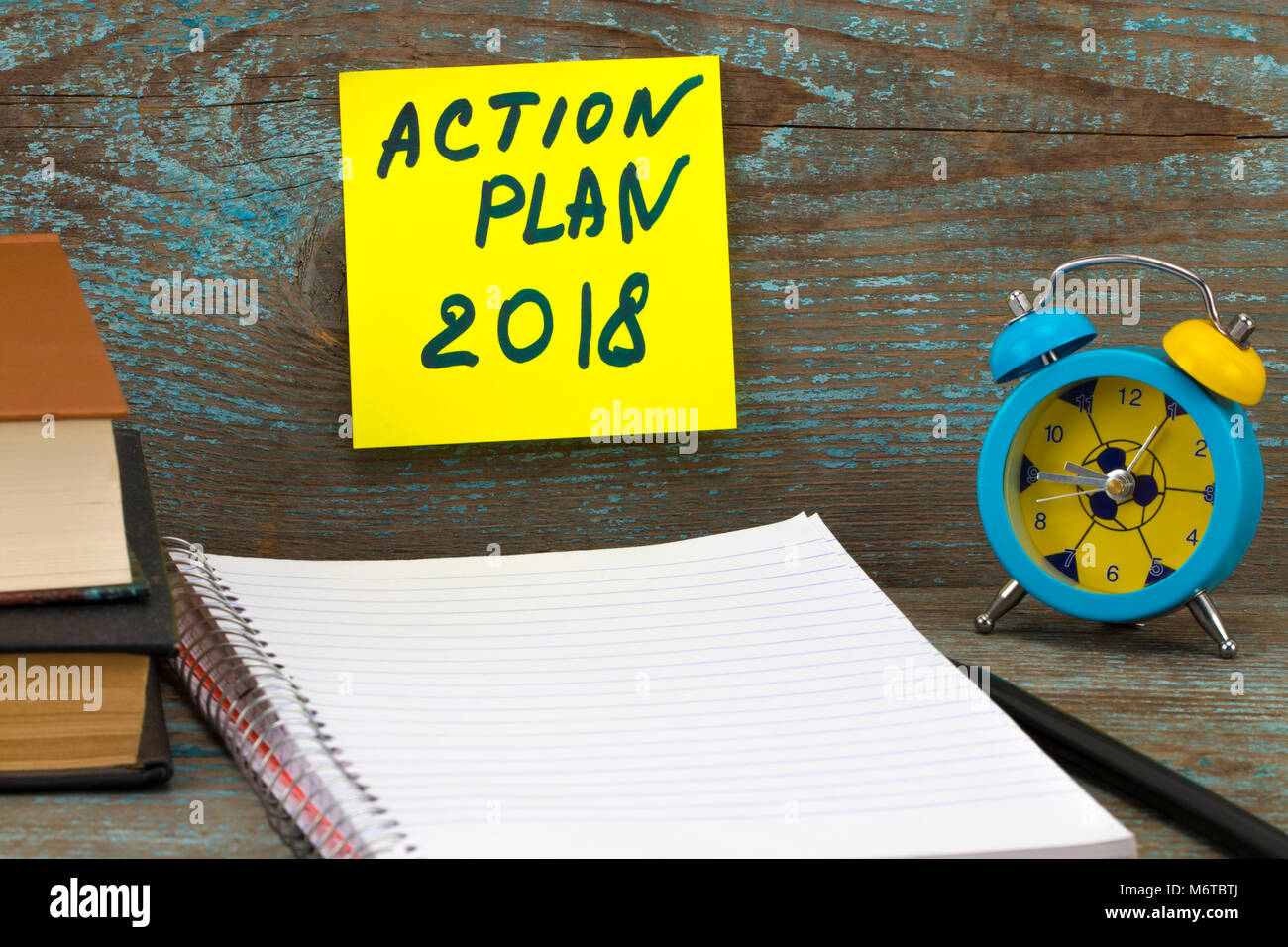 Action Plan 2018 Inscription written on sticky note. Books, pen, alarm ...