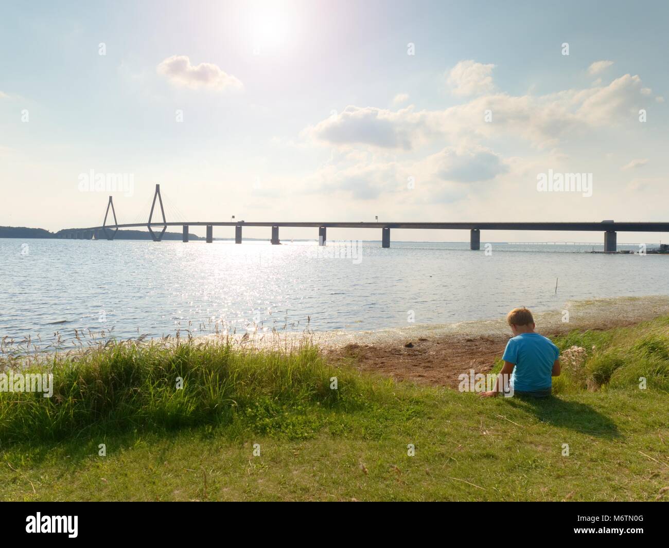 Blond hair boy is playing on sea side. Big traffic bridge between ...