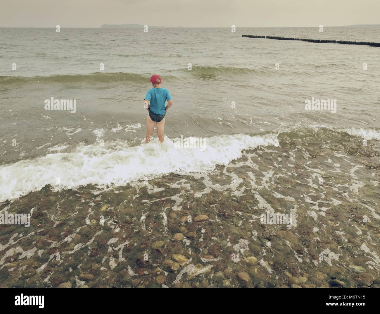 Boy in blue black sporty clothes is going into cold water of sea. Windy ...