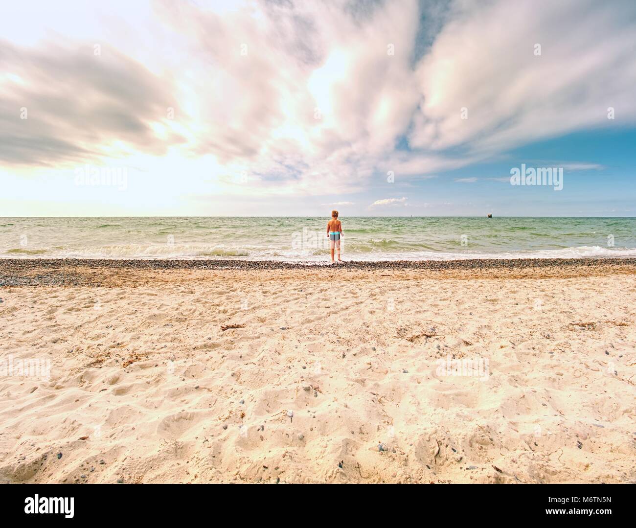 Boy in blue black sporty clothes is going into cold water of sea. Windy ...
