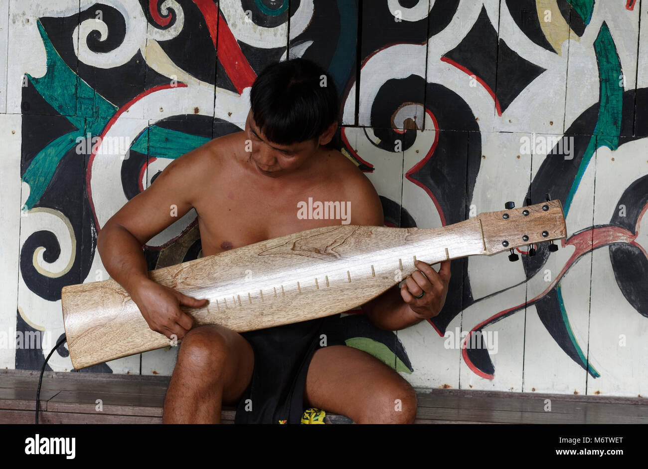 Native man playing the Sape before tree of life mural, Orang Ulu ...