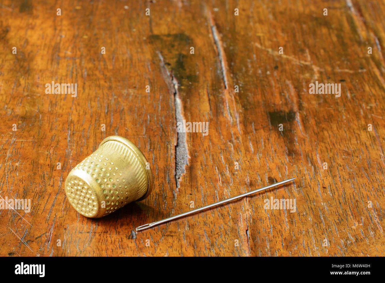 Thimble and a needle on an antique wood veneer full of cracks and ...