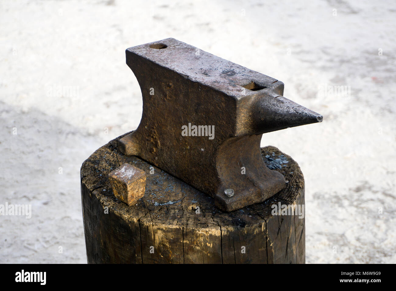 old massive iron anvil on a wooden log on a light blurred background ...