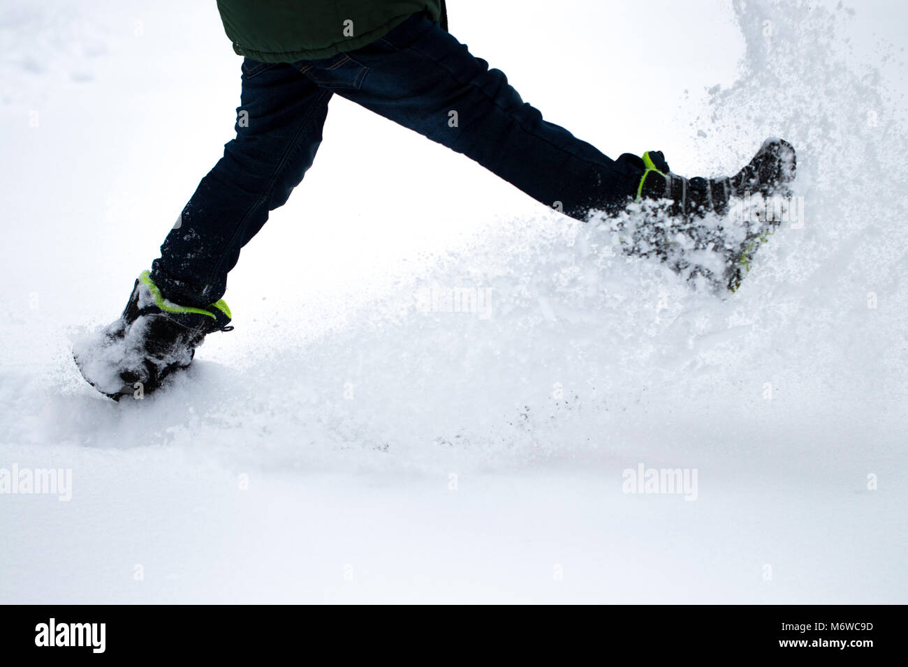 Legs of boy walks through the snow. Snow flies from under his feet ...