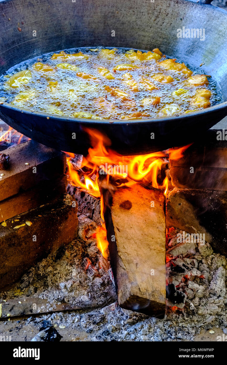 Snacks in a pan with oil are fried on open fire in the street market of ...
