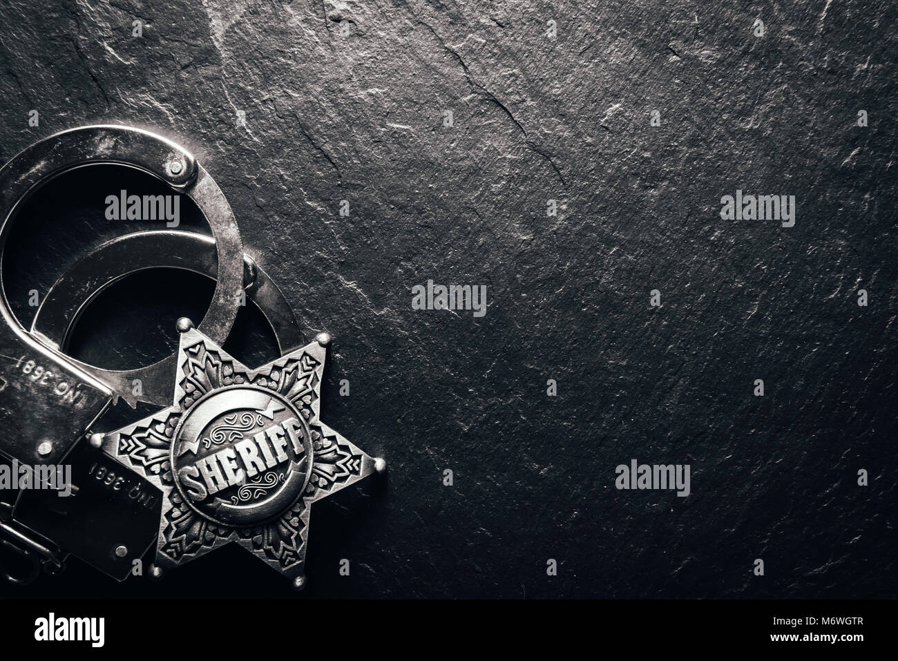 Sheriff star and handcuffs on black slate table Stock Photo - Alamy