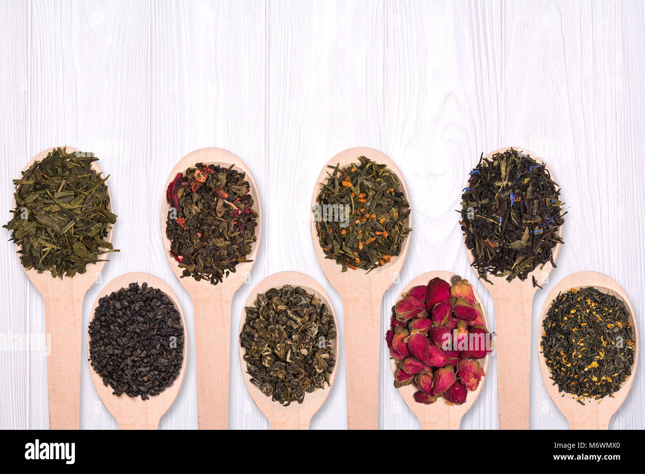 Set of different dry herbal teas in wooden spoons on a white wooden ...