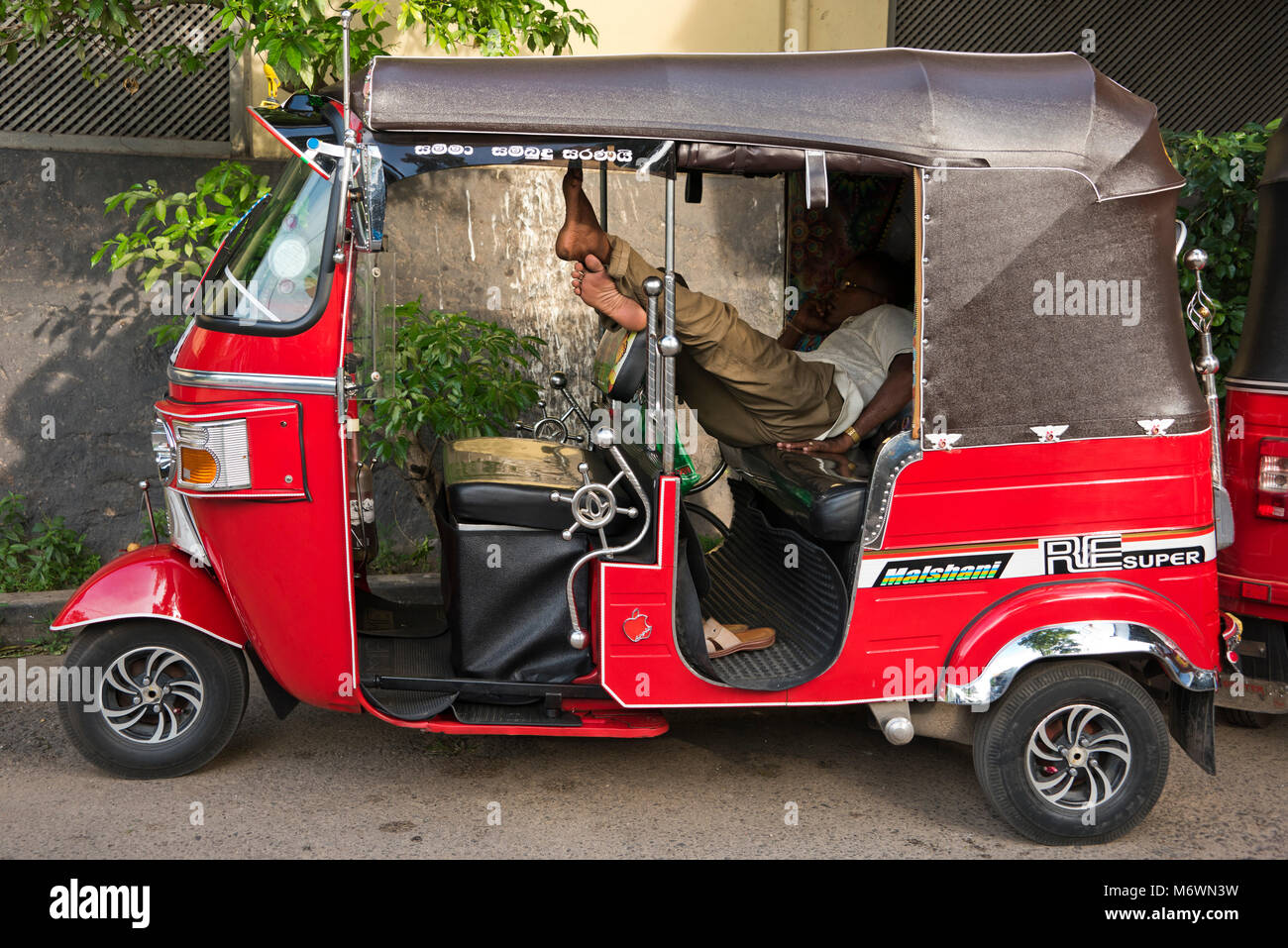 Horizontal view of a rickshaw driver asleep in the back of his vehicle ...