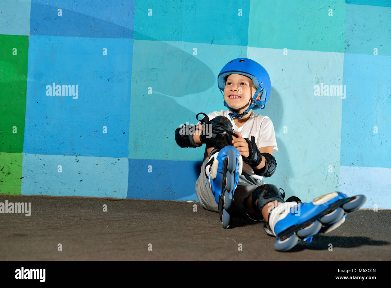 Cute little athletic boy on roller skates sitting against the blue ...