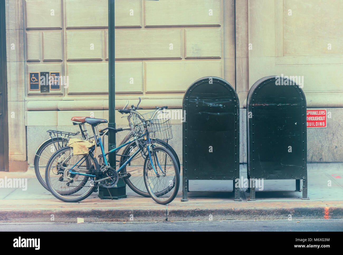 Two bicycles locked down at the light post next to the mailboxes on the ...