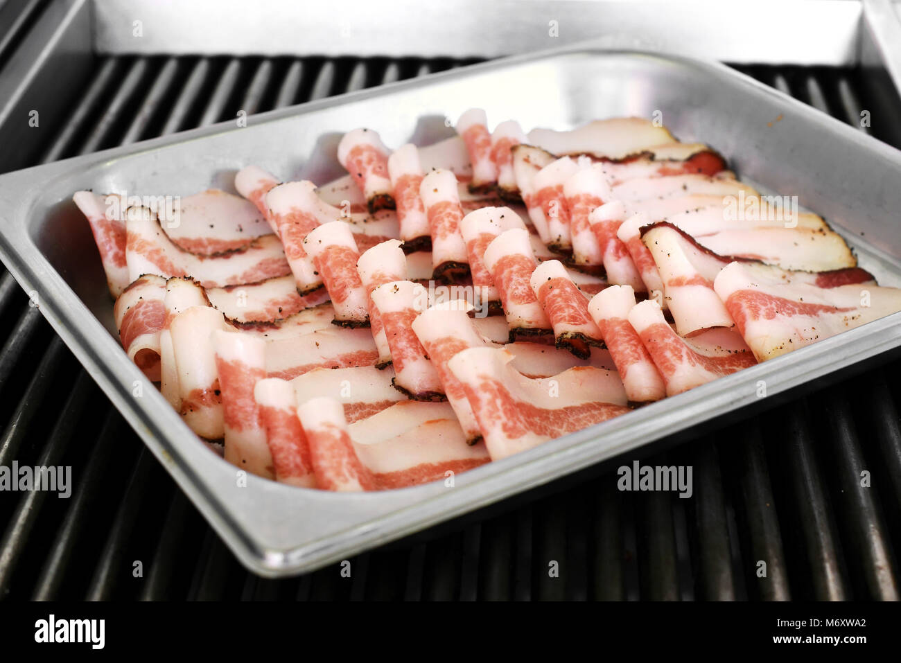 Neat rows of pre-cooked bacon slices or rashers on a metal tray in a ...