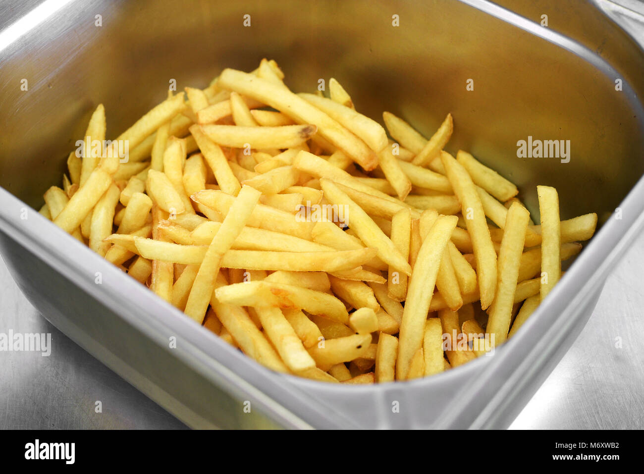 Metal bin filled with golden crispy potato chips or French fries ready ...