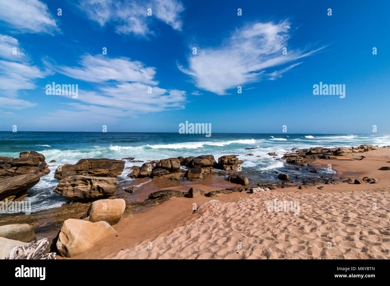 Beach sand rocks and ocean waves against blue cloud coastal skyline in ...