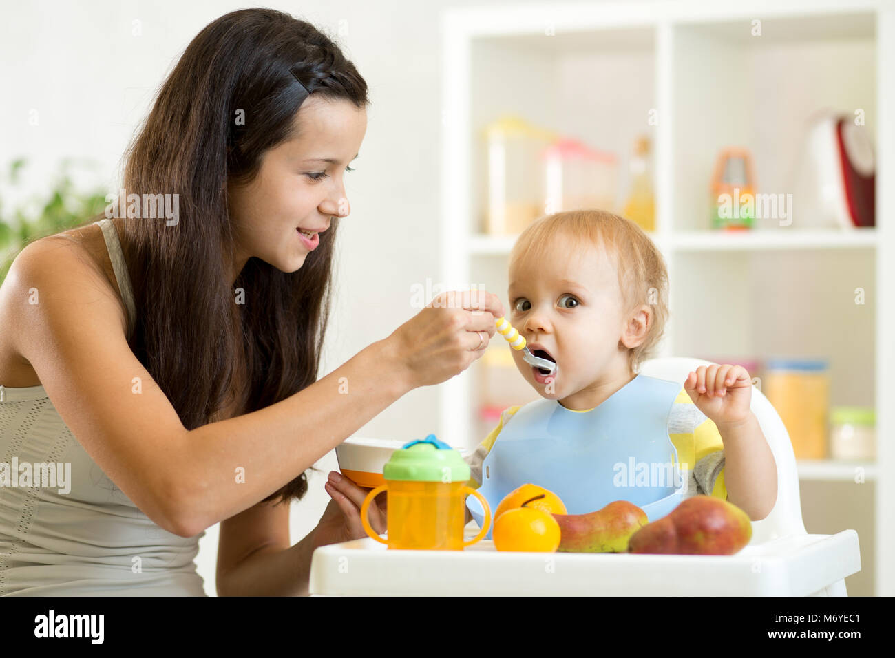 Yong mom giving homogenized food to her baby son on high chair in ...