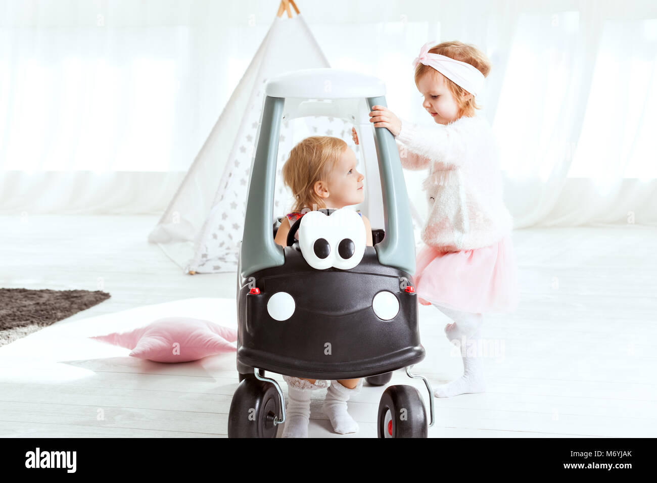 Little cute girl sitting in a toy car, her friend is standing by Stock ...