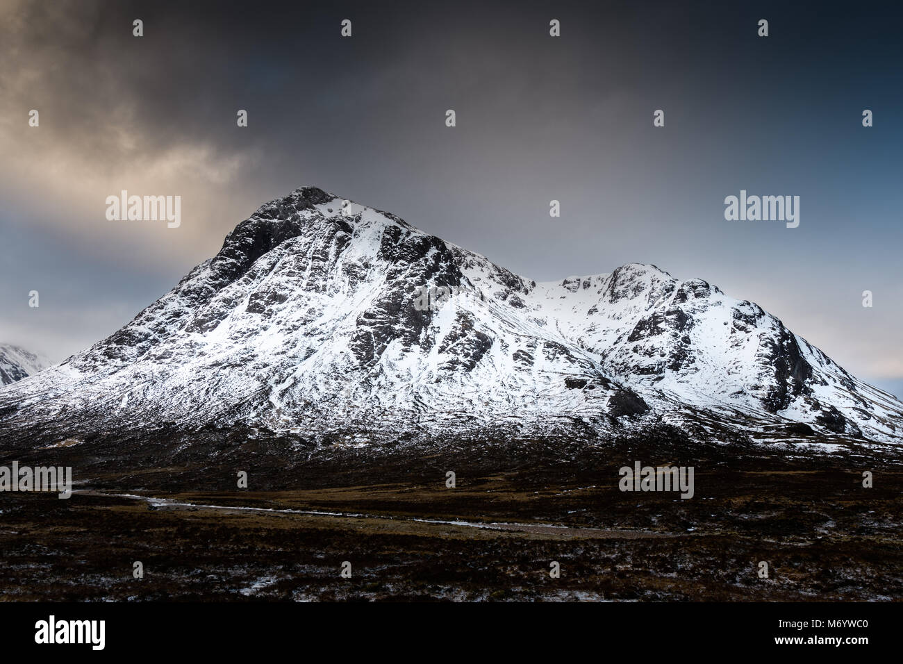 Stob Dearg mountain with snow on it an ddark clouds overhead on a cold ...